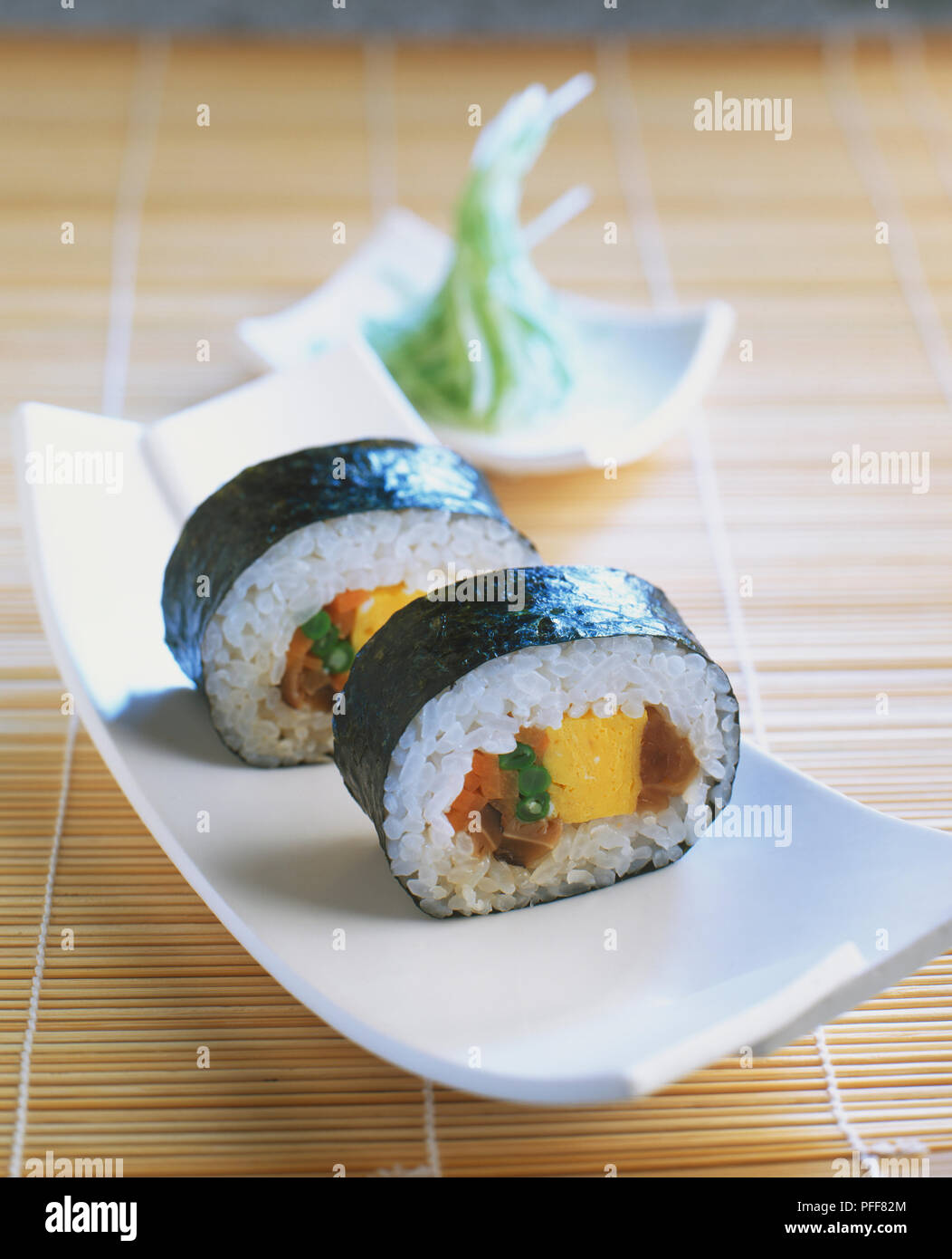 Two sushi parcels on curved plate, green vegetable parcel on smaller ...