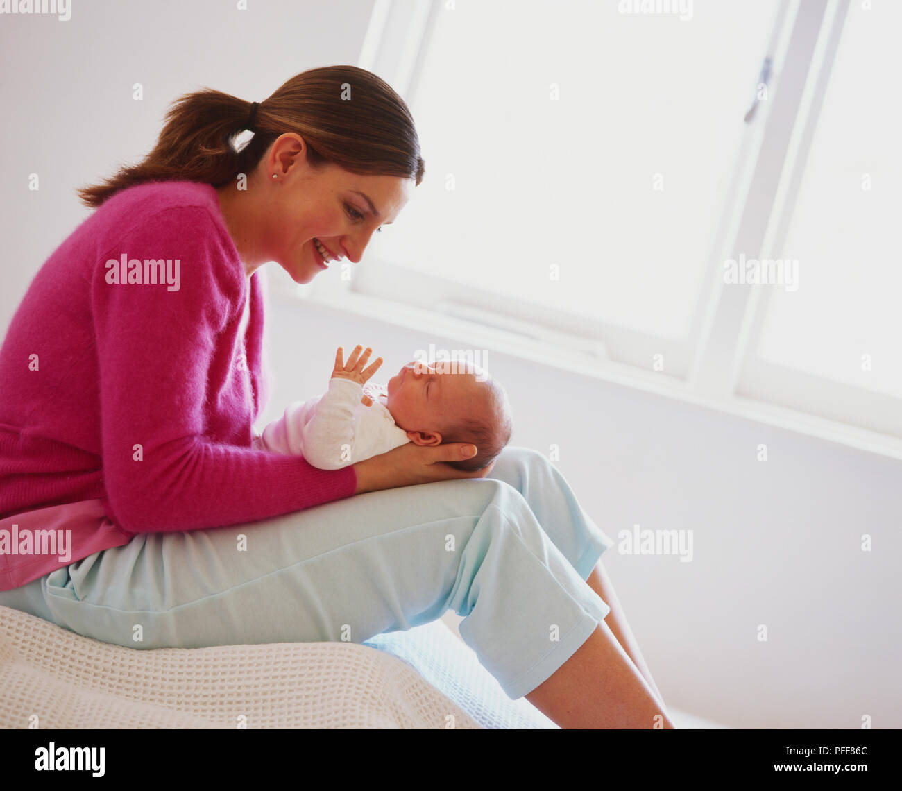 Woman holding young baby, in her lap, supporting its head with her ...
