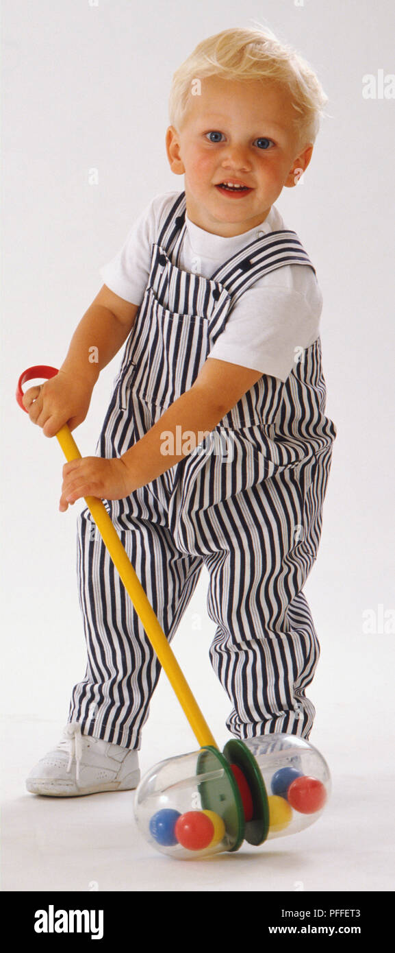 Toddler standing, pushing a transparent rattle ball with a long wooden ...