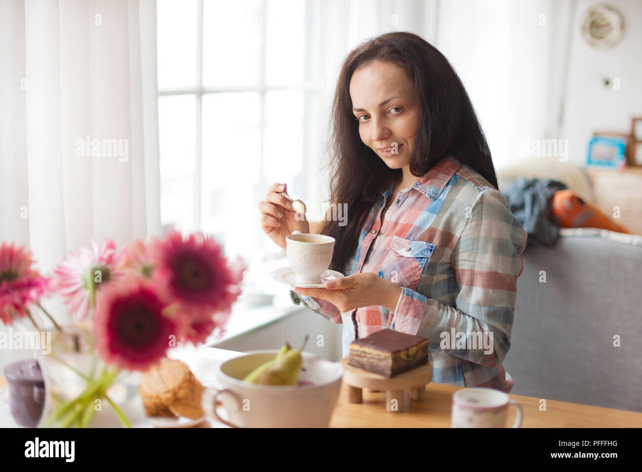 A woman is eating breakfast at the window, on the table a bouquet of ...