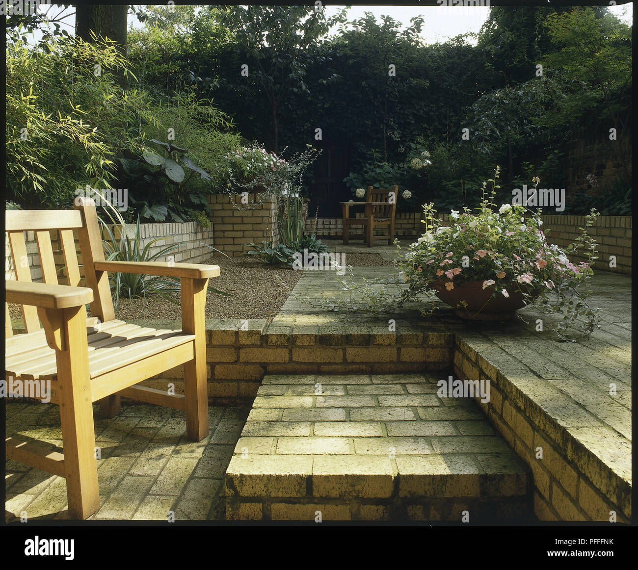 Town garden patio with brick steps, pot plants and wooden garden bench ...
