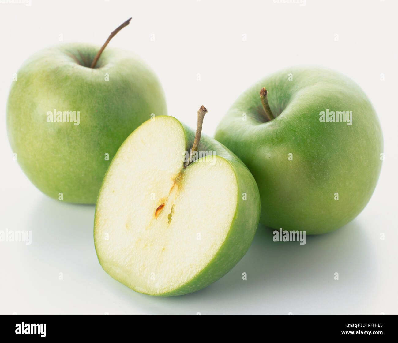 Two whole and one halved green apple, showing cross section of fruit ...