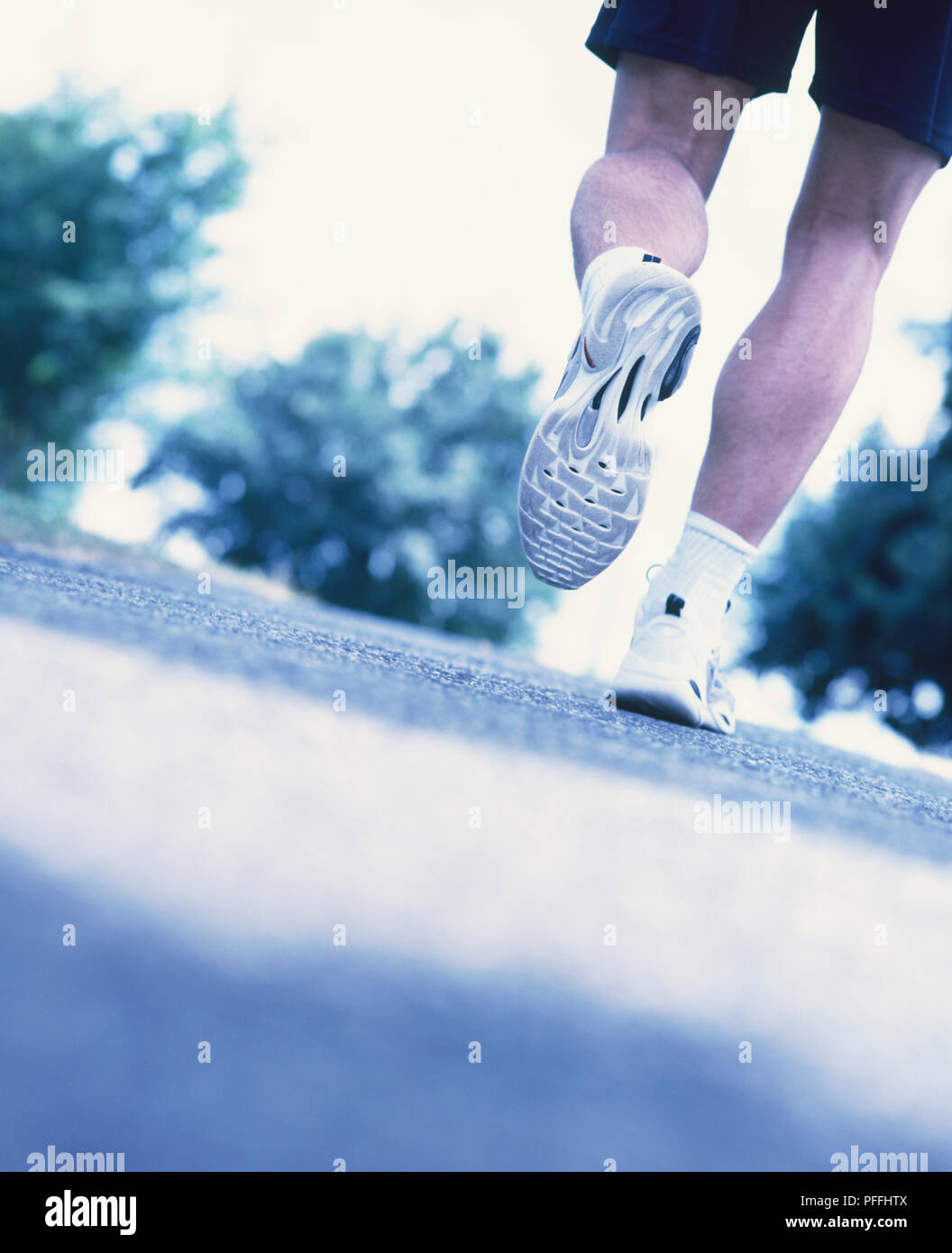 Rear view of the lower part of a pair of legs, wearing trainers ...