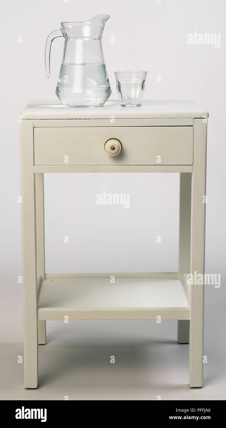 Wooden, painted bedside table with glass jug of water and glass of ...