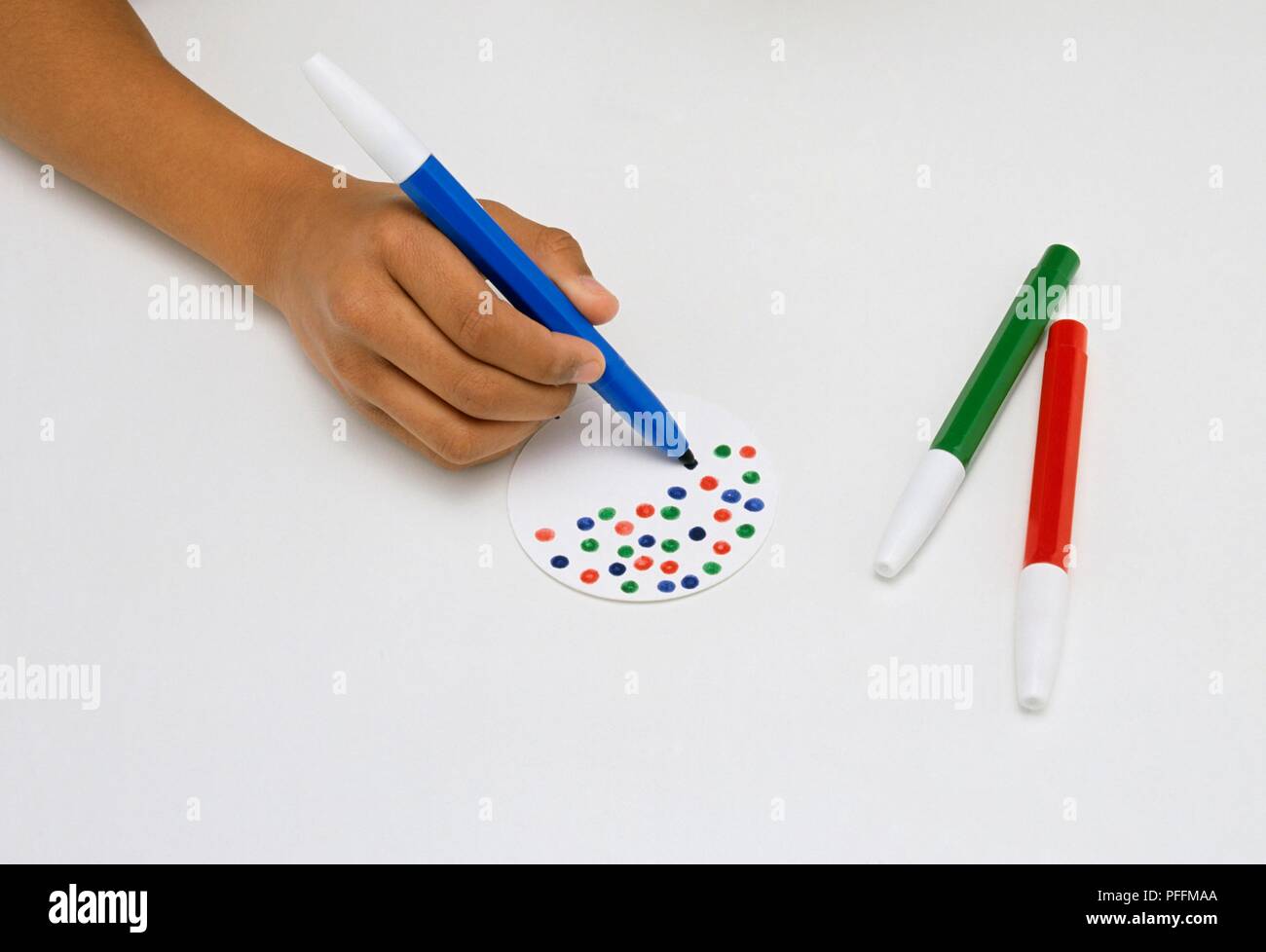 Child using blue, green and red felt tip pens to draw coloured spots on ...