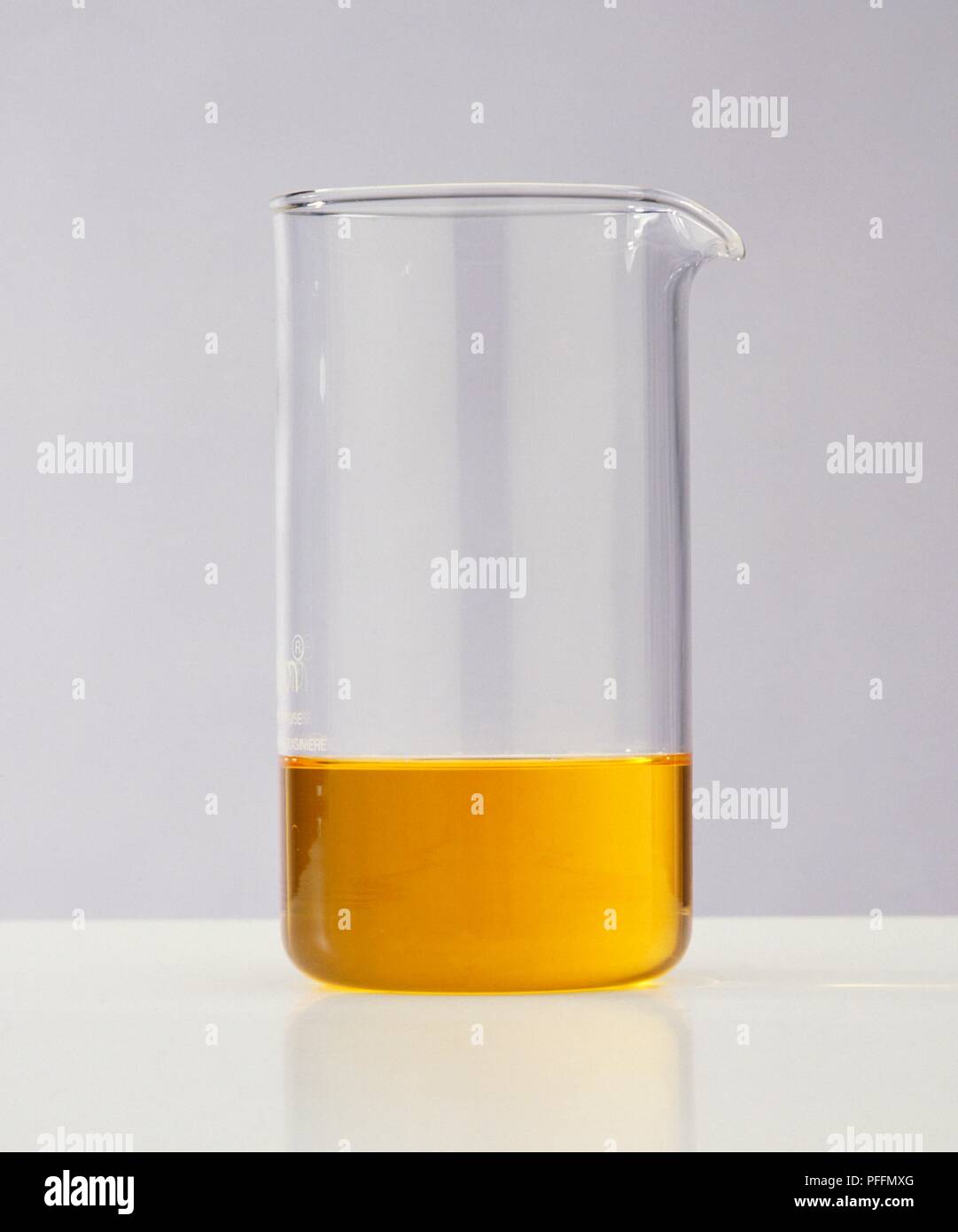 A glass beaker containing a small measure of a gold coloured ...