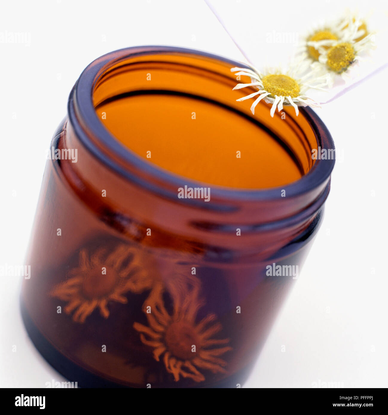 Roman Chamomile flower heads inside and on edge of brown glass jar ...