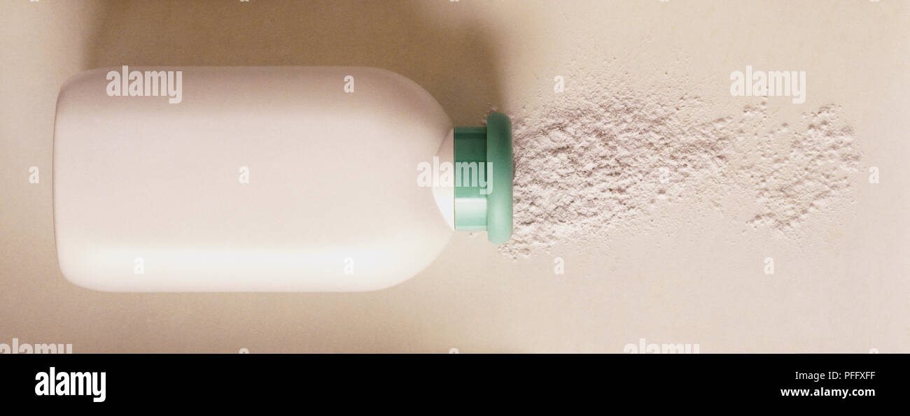 A white bottle with green lid on its side and some white powder spilt ...