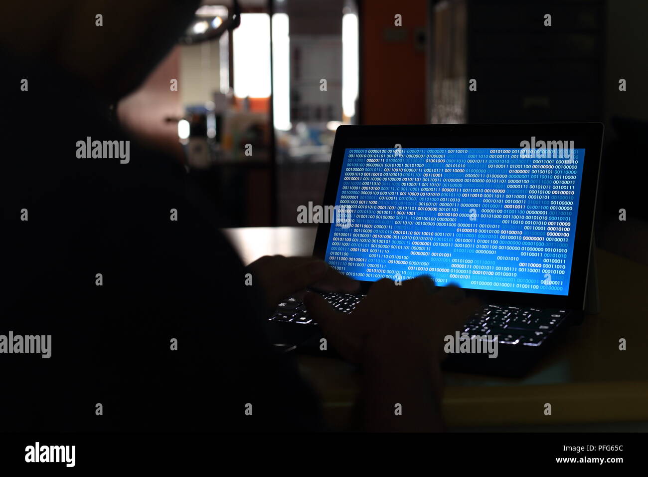 Computer Hacker silhouette typing on computer in a dark room. Working on blue binary code ...