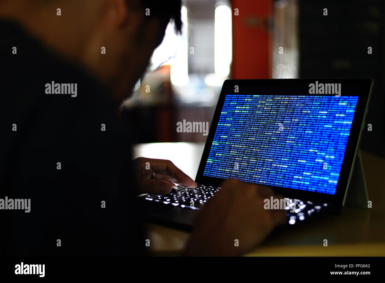 Computer Hacker silhouette typing on computer in a dark room. Working on blue binary code ...