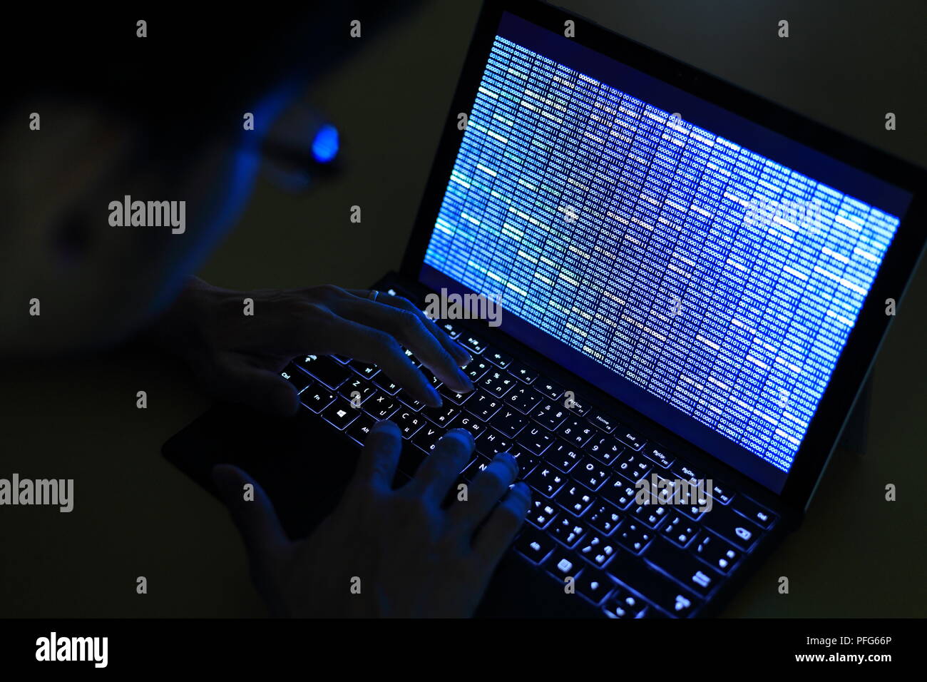 Computer Hacker silhouette typing on computer in a dark room. Working on blue binary code ...