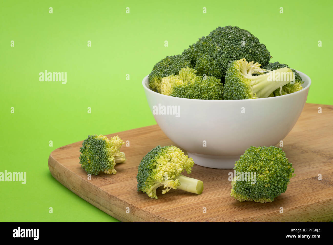 Broccoli pieces in white bowl sitting on wooden chopping board Stock ...