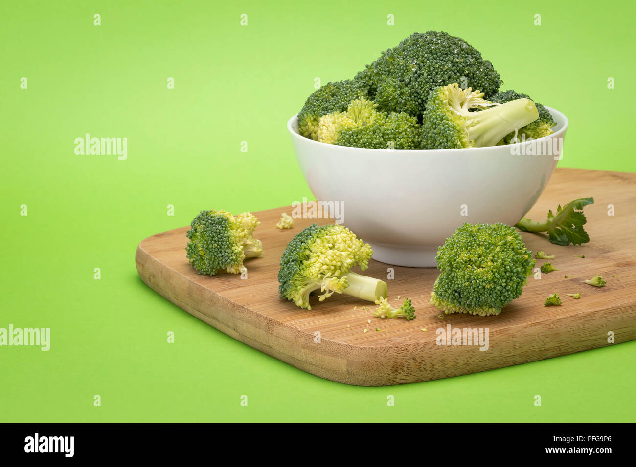 Broccoli pieces in white bowl sitting on wooden chopping board Stock ...