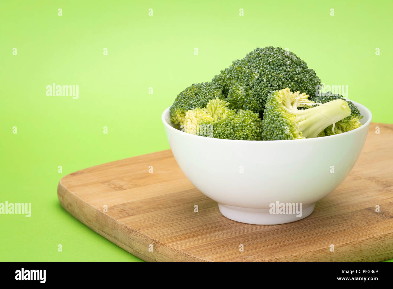 Broccoli pieces in white bowl sitting on wooden chopping board Stock ...