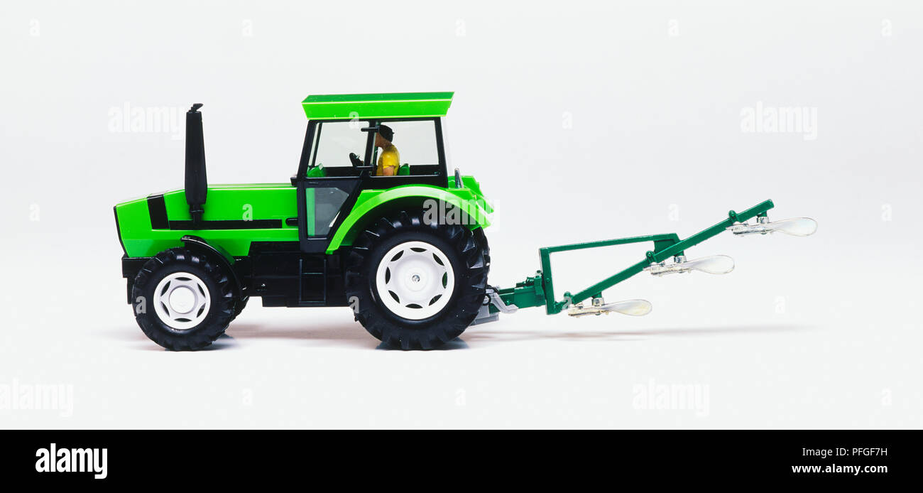 Green toy tractor pulling plough, side view Stock Photo - Alamy