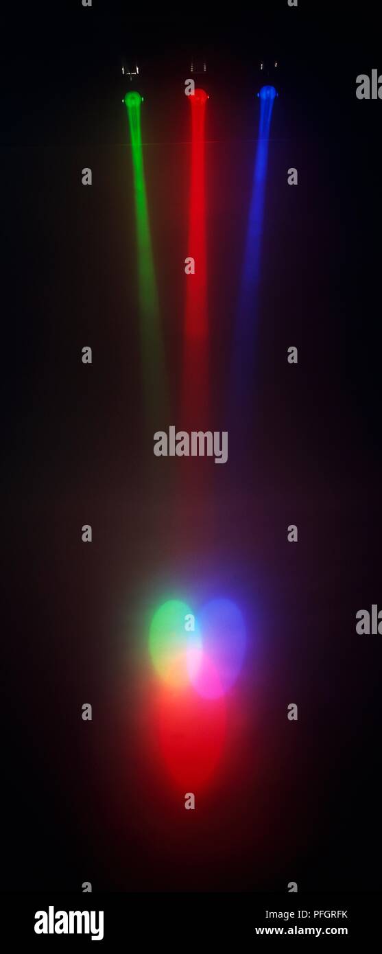 Rays of different coloured lights merging together on a black ...