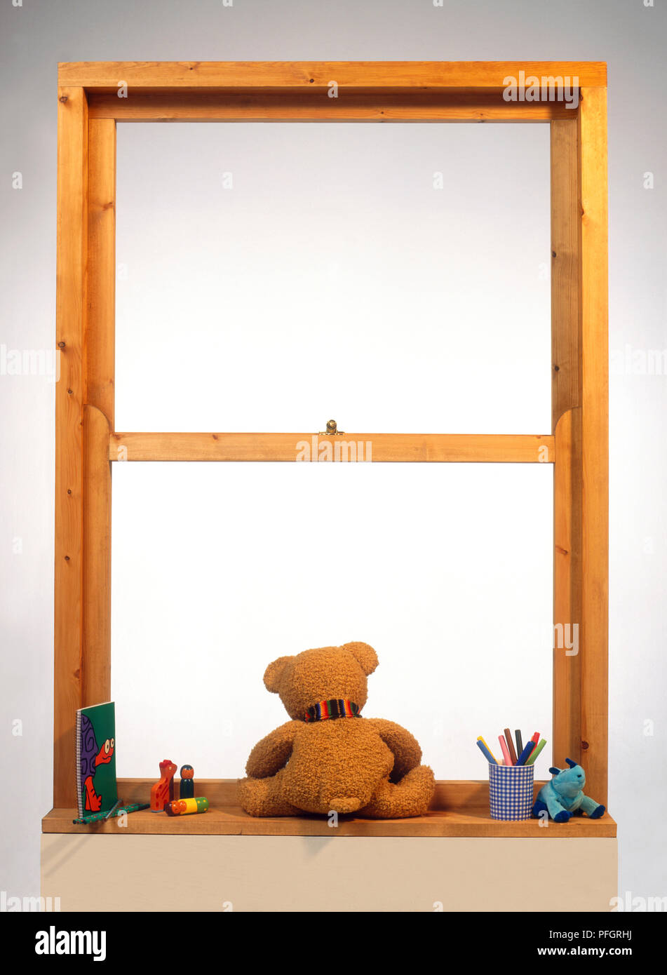 Rear view of a teddy bear sitting on the sill of a window frame ...