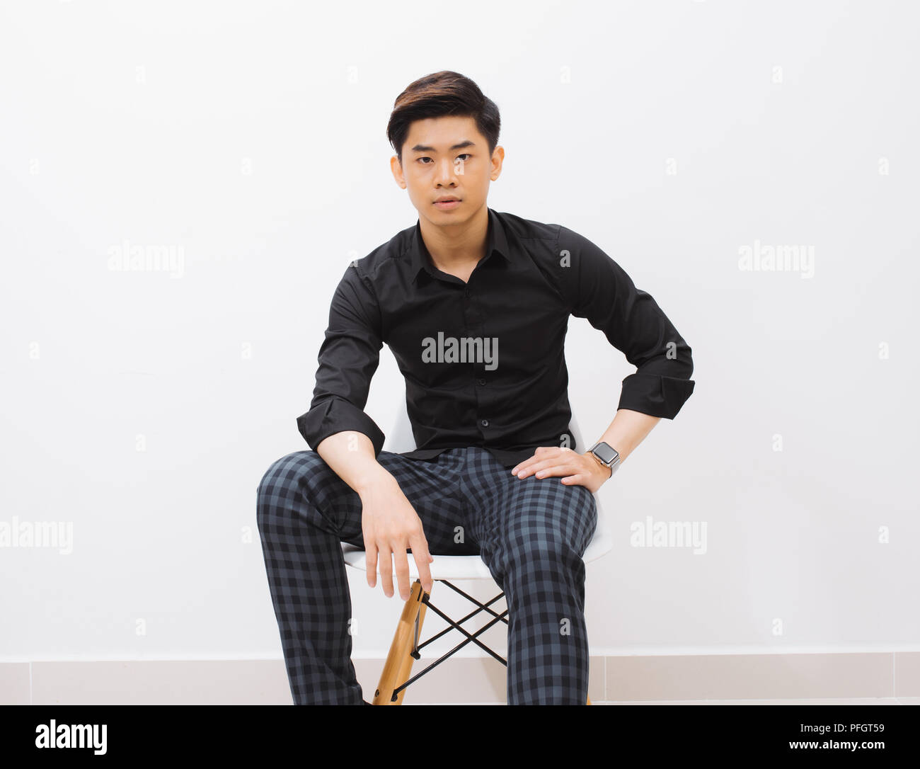 Casually handsome. Studio shot of handsome young man sitting on the chair and looking at camera ...