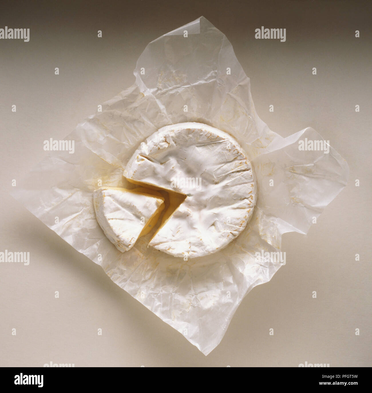 Round block of Camembert Cheese on opened wrapper with cut section ...