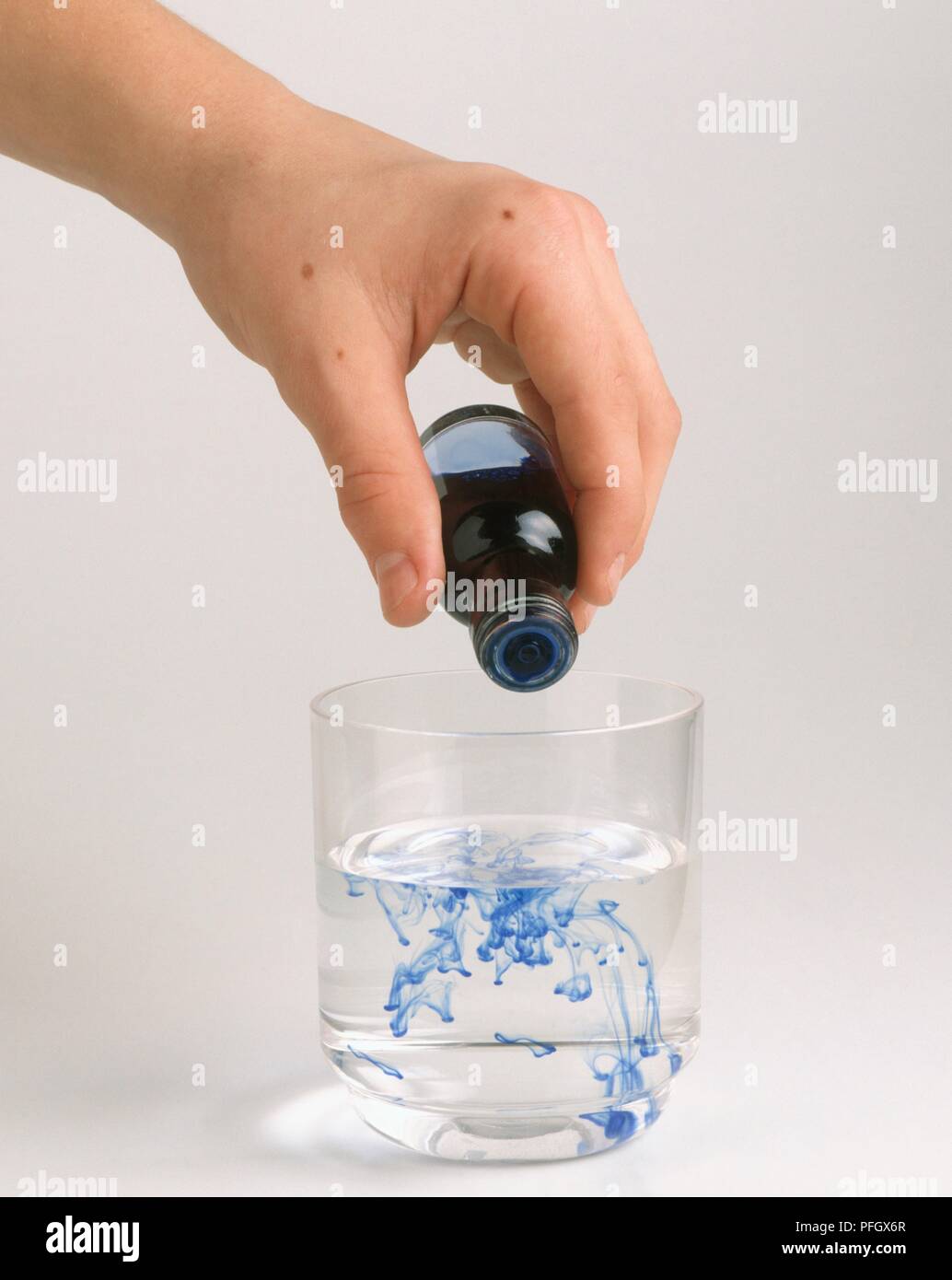 Hand pouring food colouring into glass of water Stock Photo - Alamy