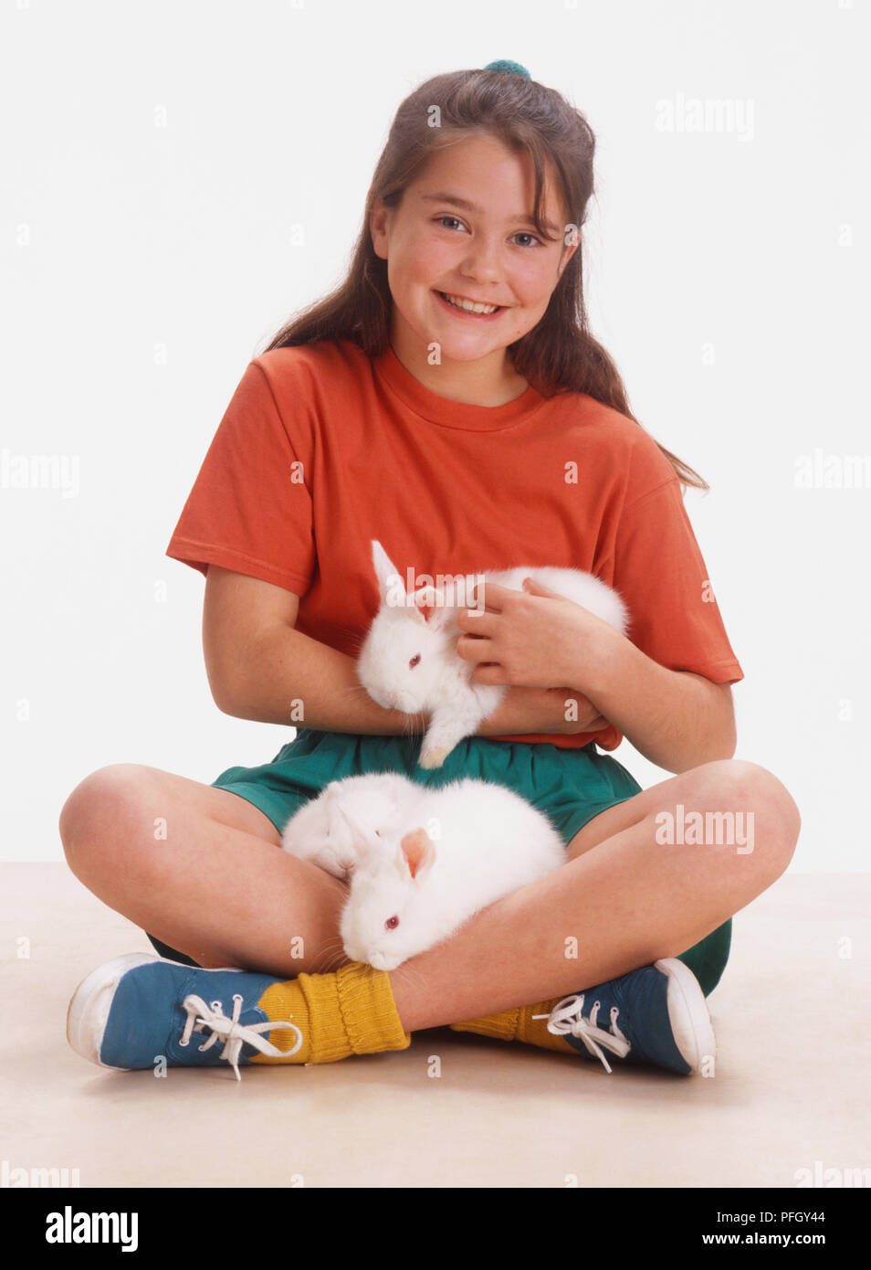 Smiling girl sitting cross-legged on the floor holding white Rabbit ...
