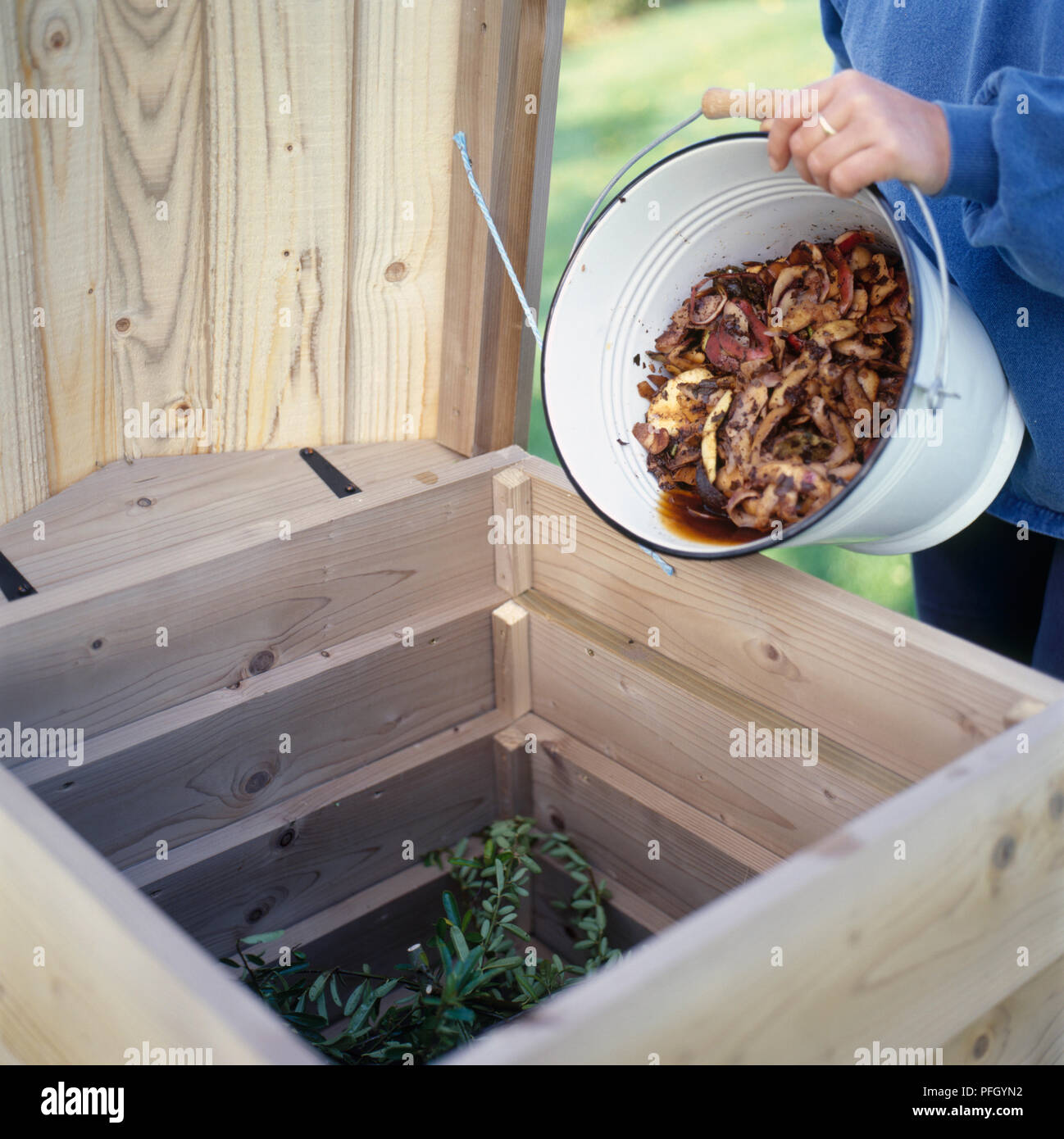 Tipping organic waste from metal bucket into wooden compost bin, close ...