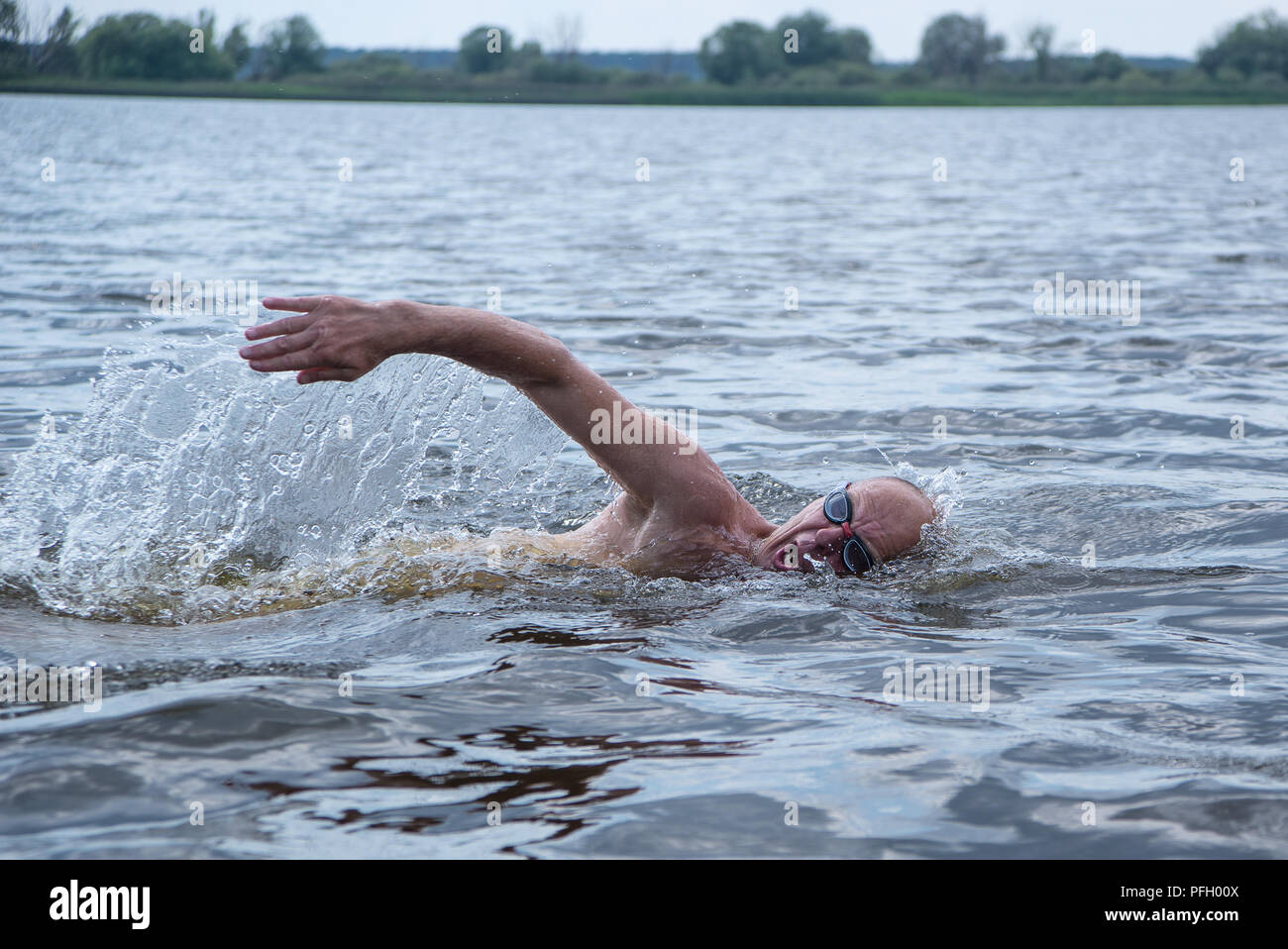 An elderly muscular man in swimming goggles swims with a crawl style ...