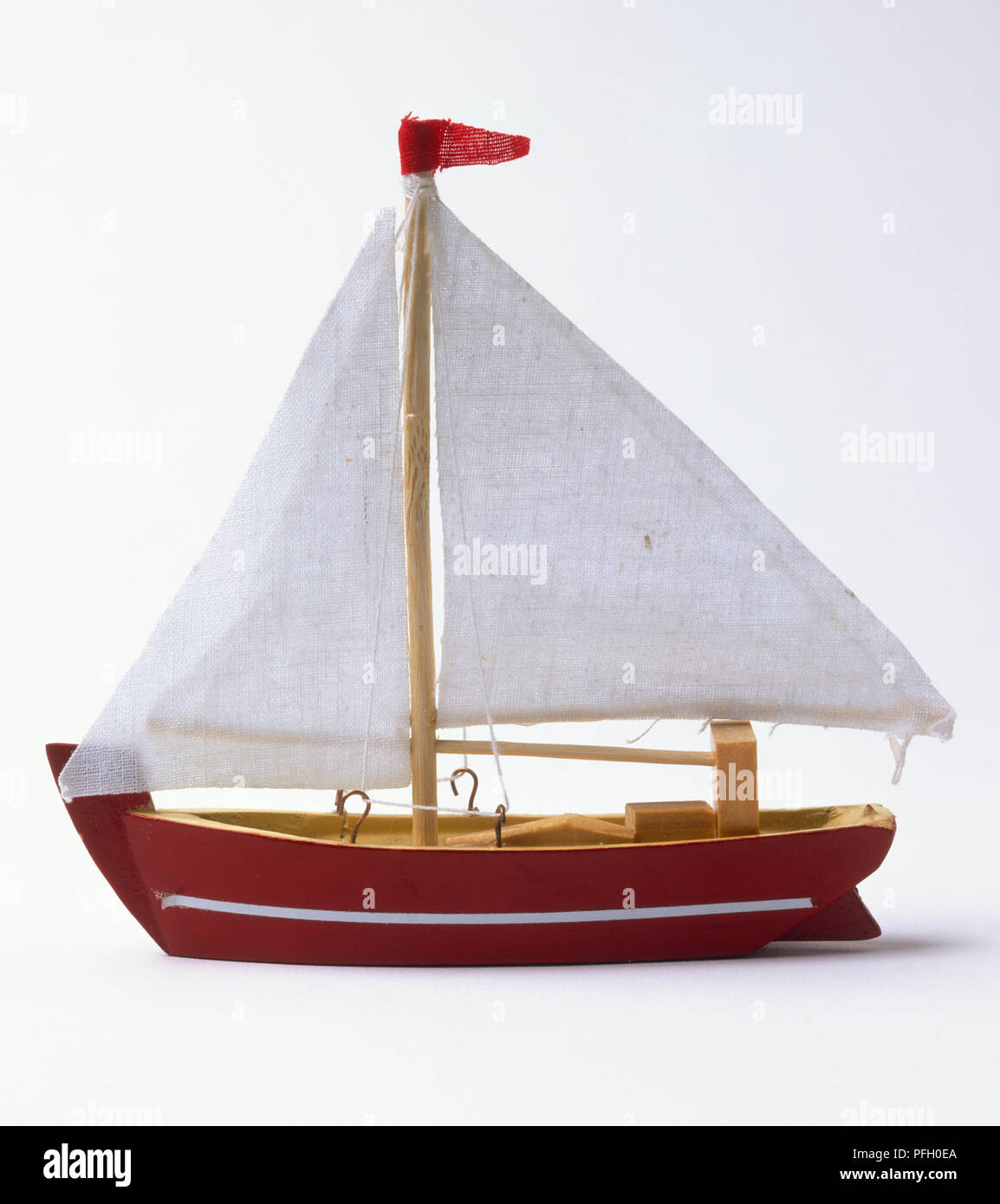 Wooden red toy boat with white sail and a white stripe across the hull ...