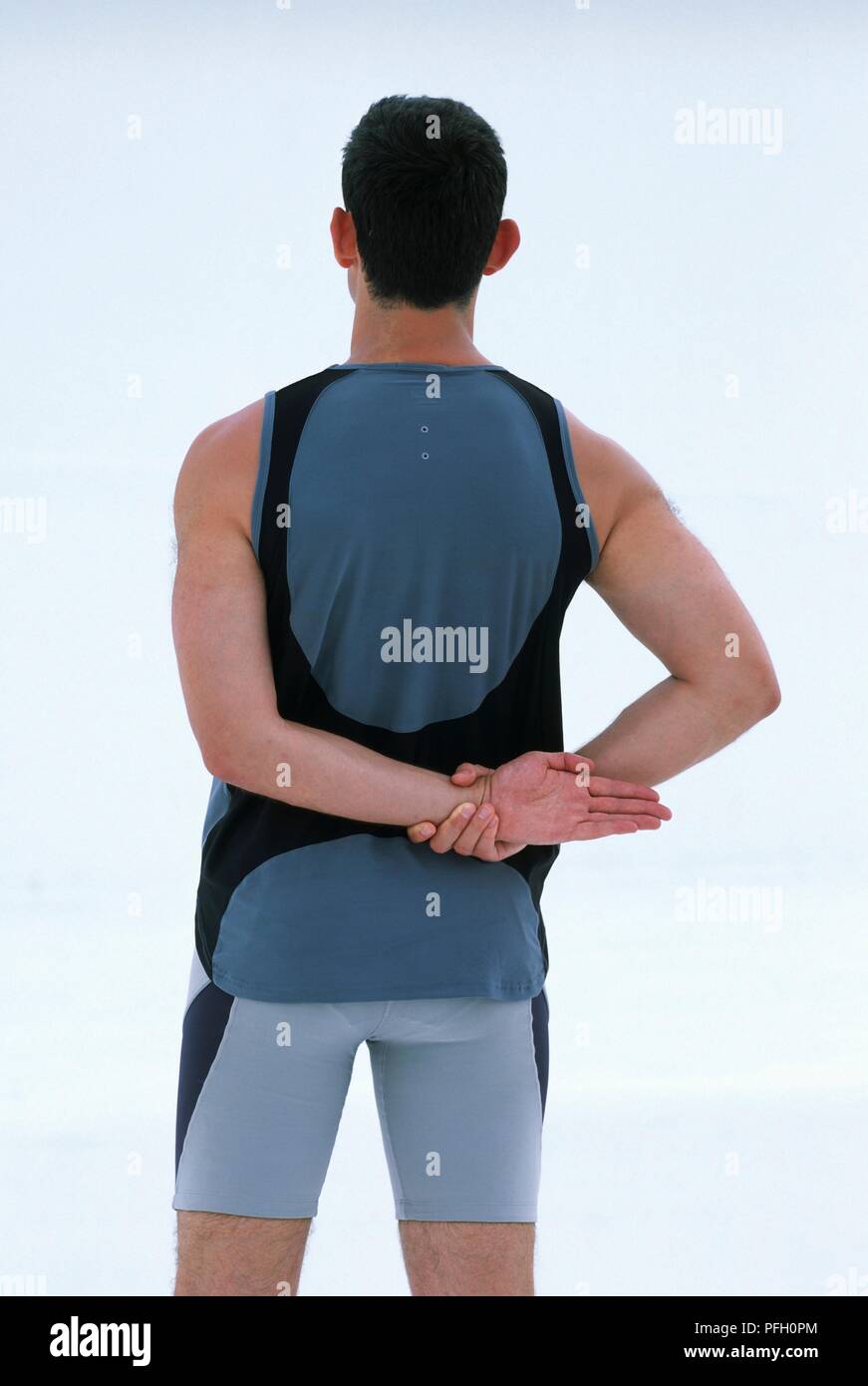 Man in grey shorts and tank top stretching his arms behind his back ...