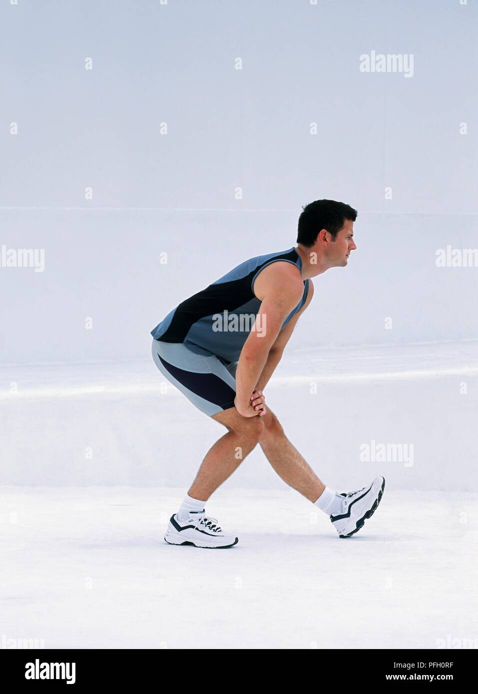Man in shorts and tank top leaning forward with one leg stretched ...