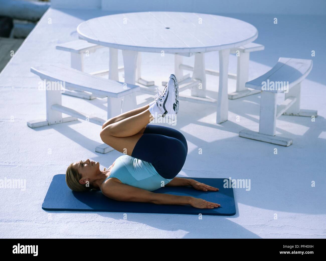 Woman lying on back on exercise mat with her body rolled back and feet ...
