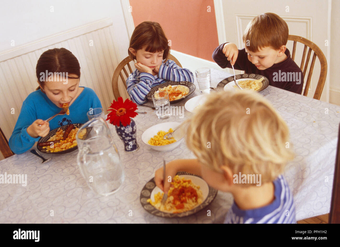 Four children around a table eating pasta Stock Photo - Alamy