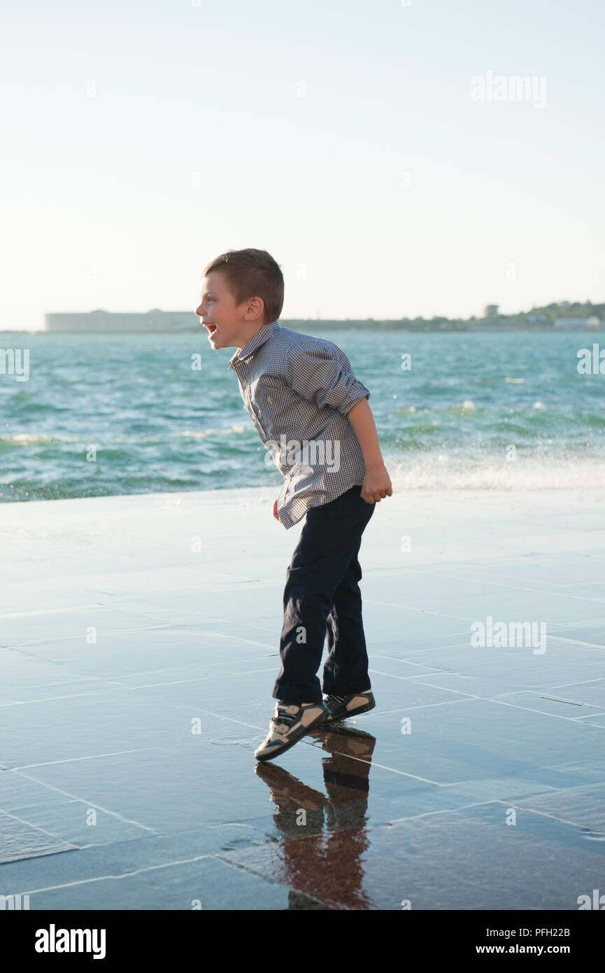funny jumping little boy shouting towards storm sea in port town in ...