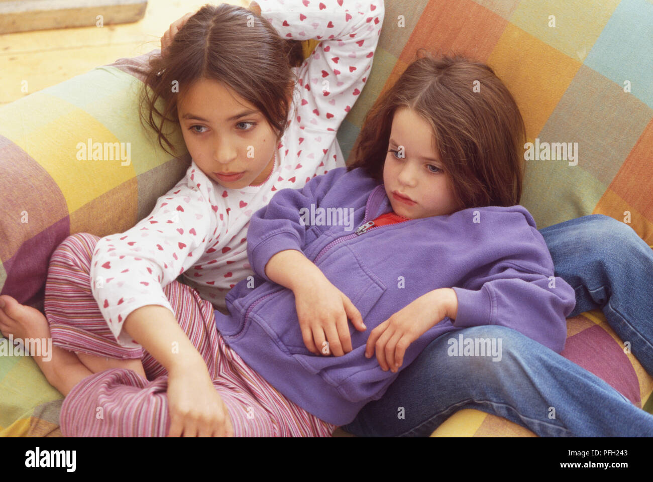 Girl sitting crossed-legged on another girl casually slumped of an arm ...