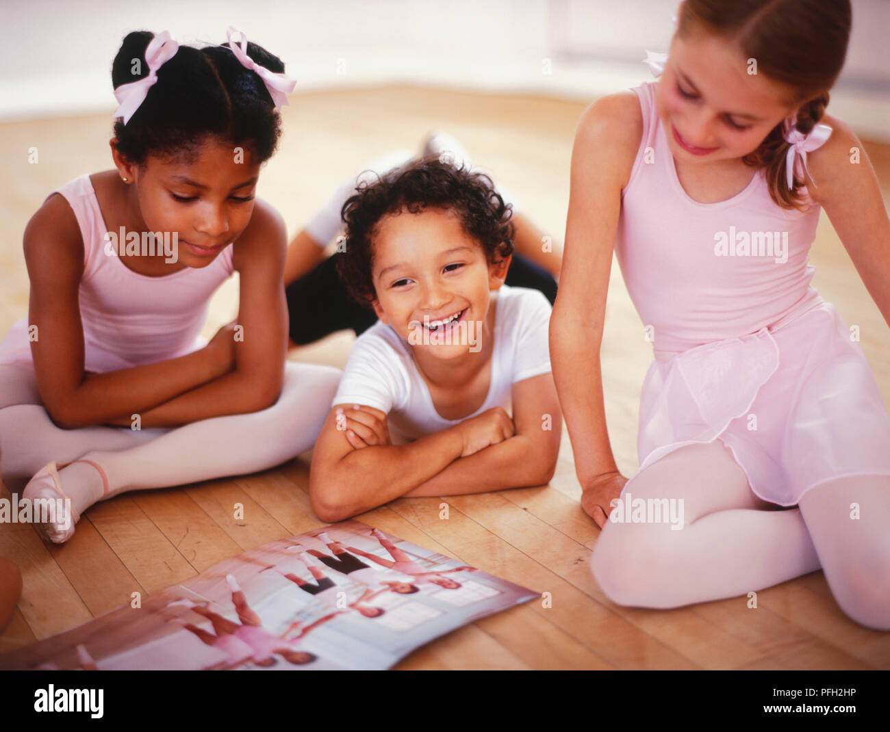 Three young ballet dancer lounging on floor reading magazine Stock ...