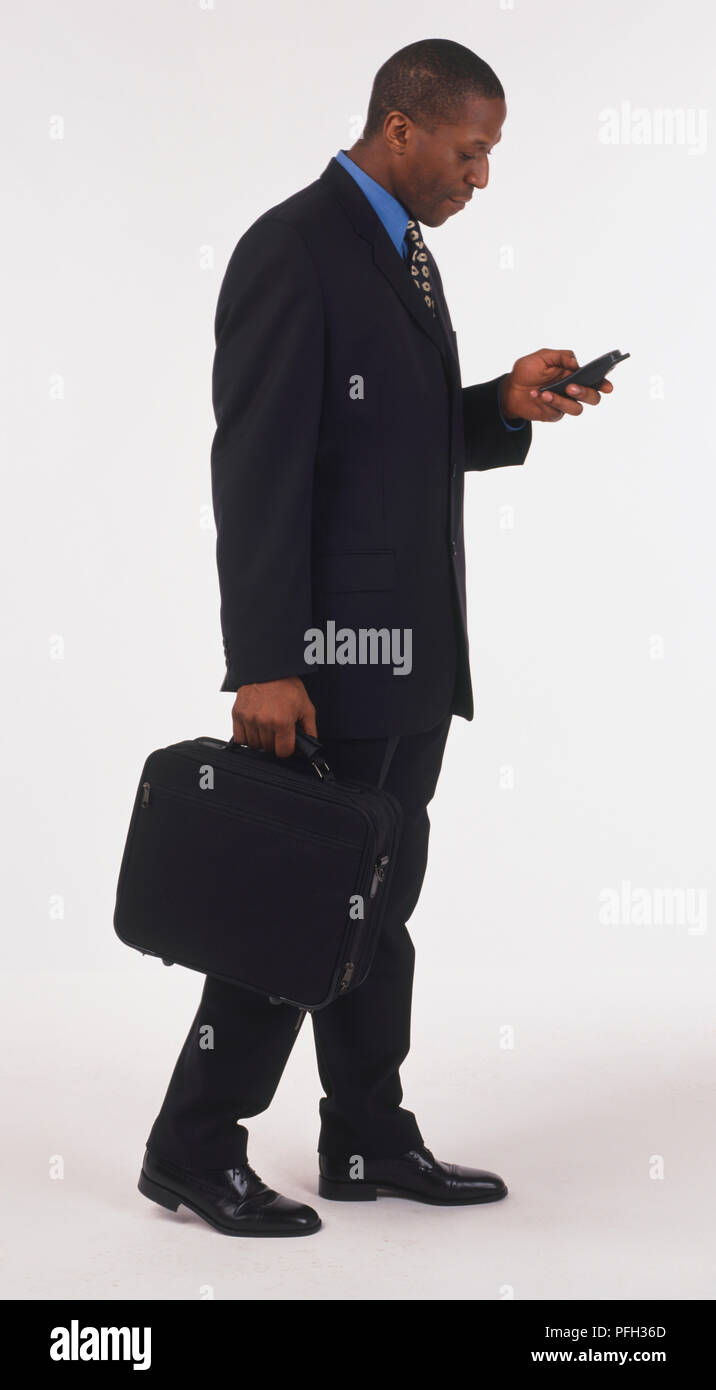 Man in business suit holding a mobile phone in one hand and carrying a ...