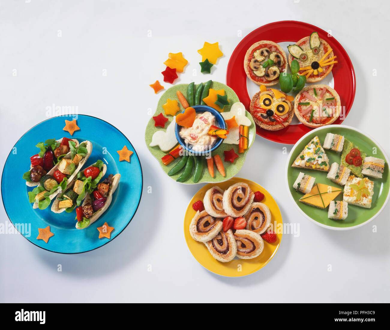 Selection of party snacks laid out on five colourful plates, view from ...