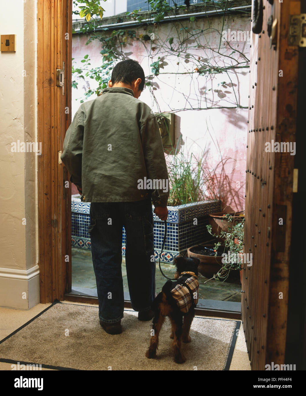 Boy holding a dog on a leash standing in door frame of an open front ...