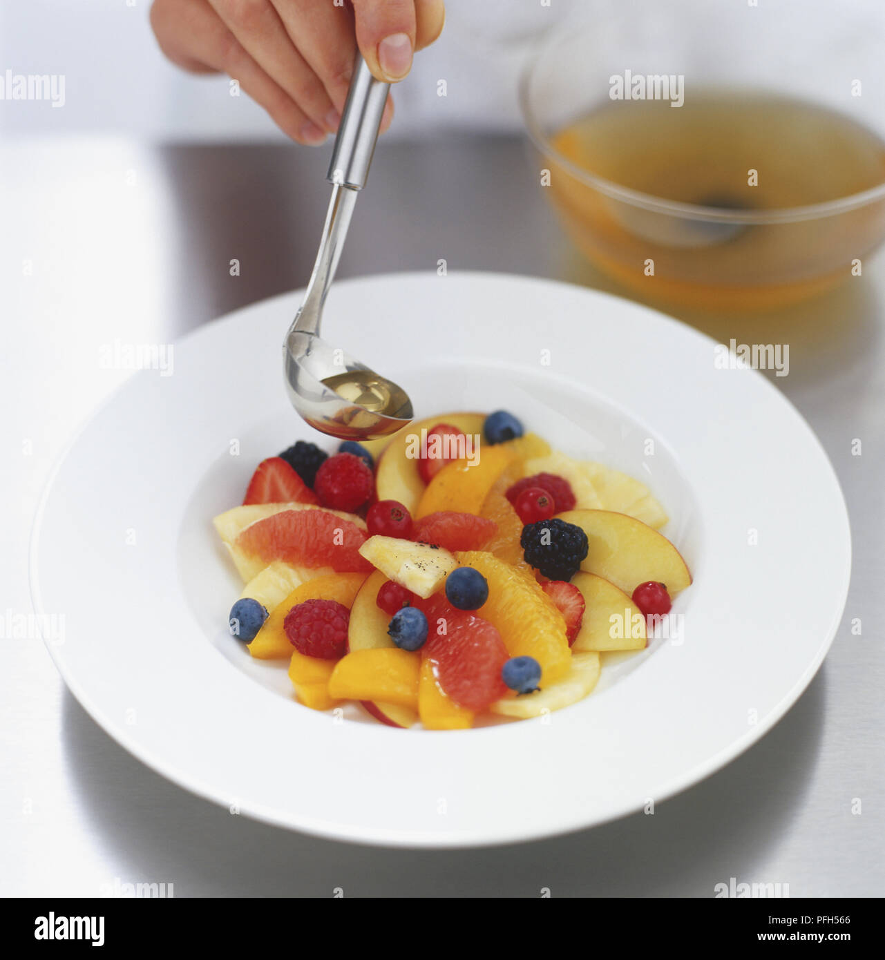 Spooning syrup over fruit salad served in a shallow plate Stock Photo ...