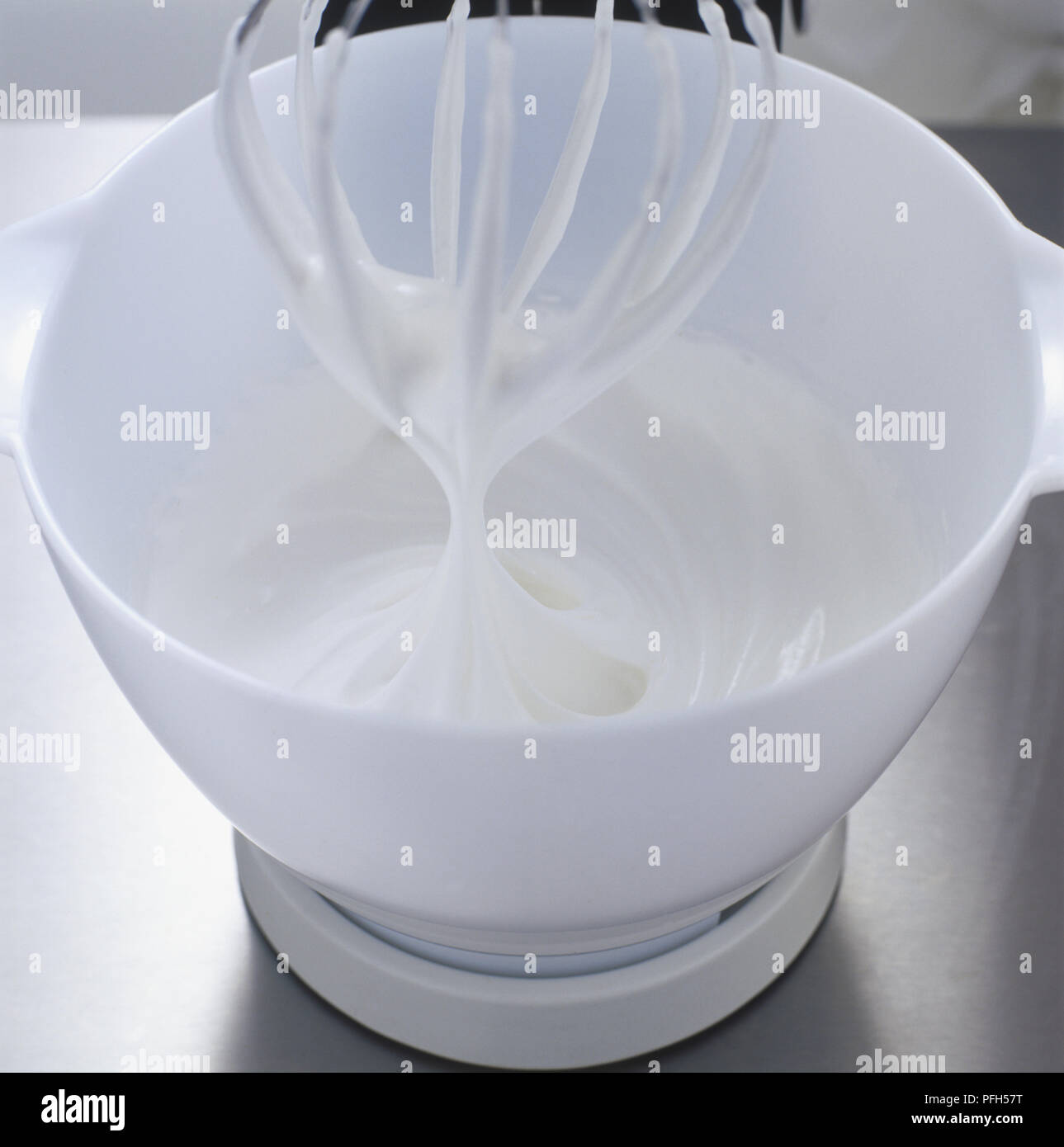 Metal whisk being lifted up from bowl of Italian meringue, high angle ...
