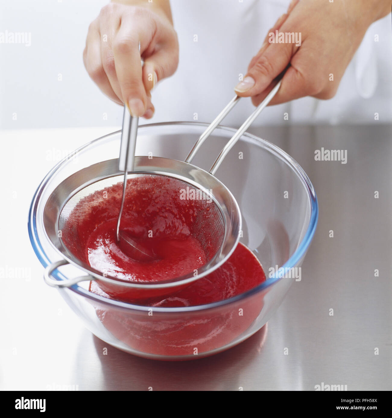 Straining raspberry puree into glass bowl through seive Stock Photo - Alamy