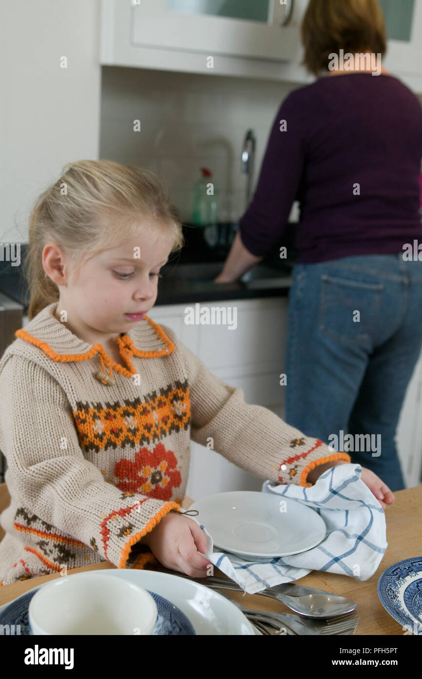 Girl drying plates, woman washing plates in background Stock Photo - Alamy