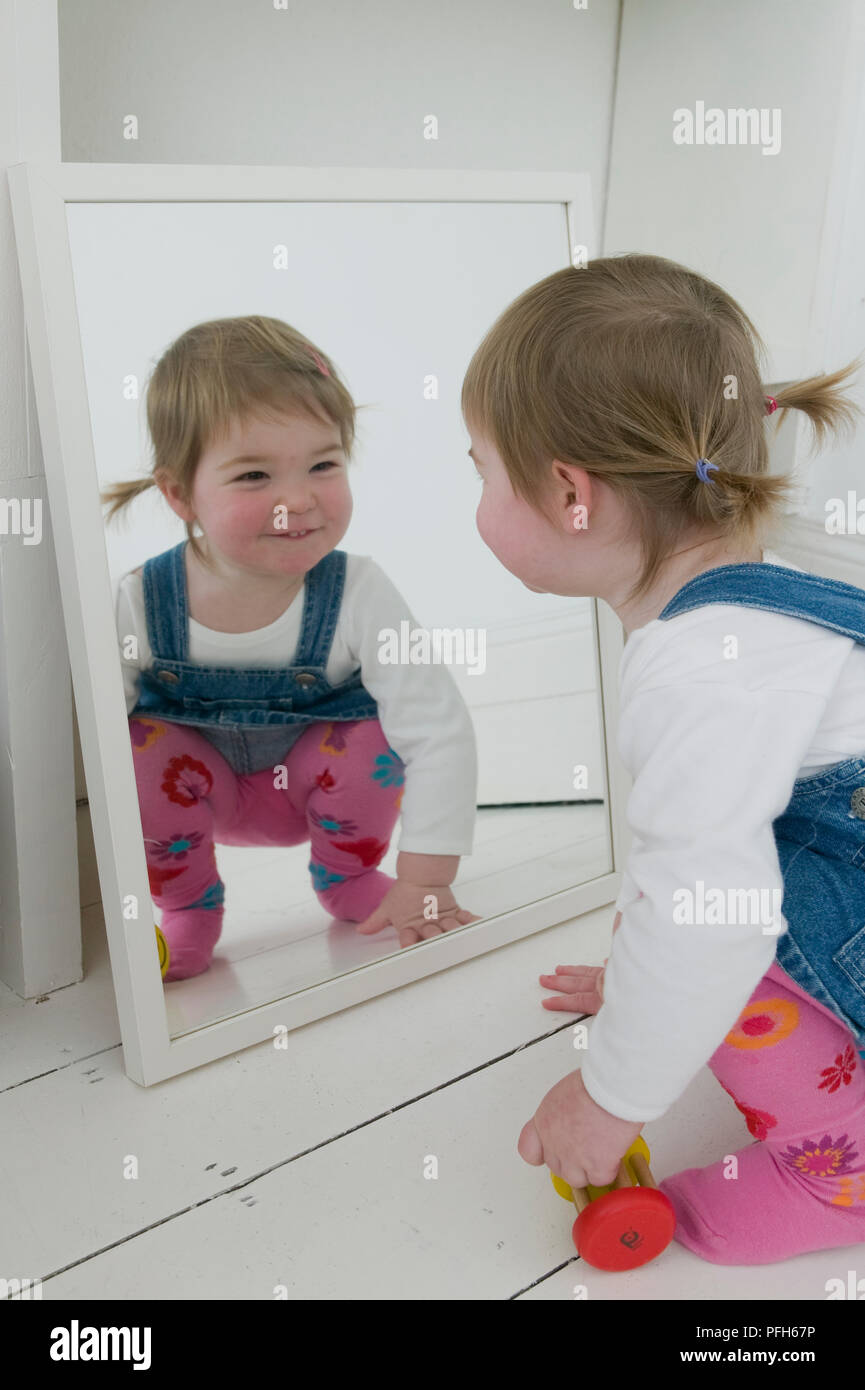 Girl crouching and looking in mirror, smiling Stock Photo - Alamy