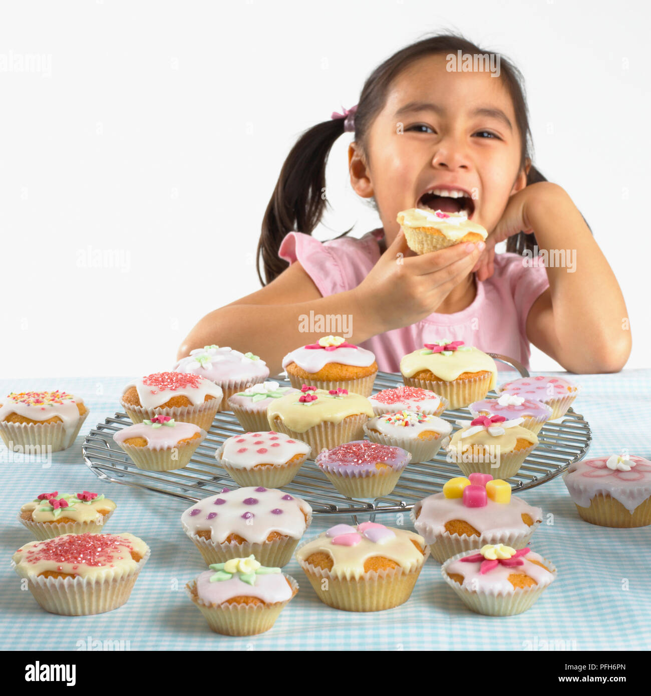 Girl eating a cupcake, more cupcakes on a cooling rack in front of her ...
