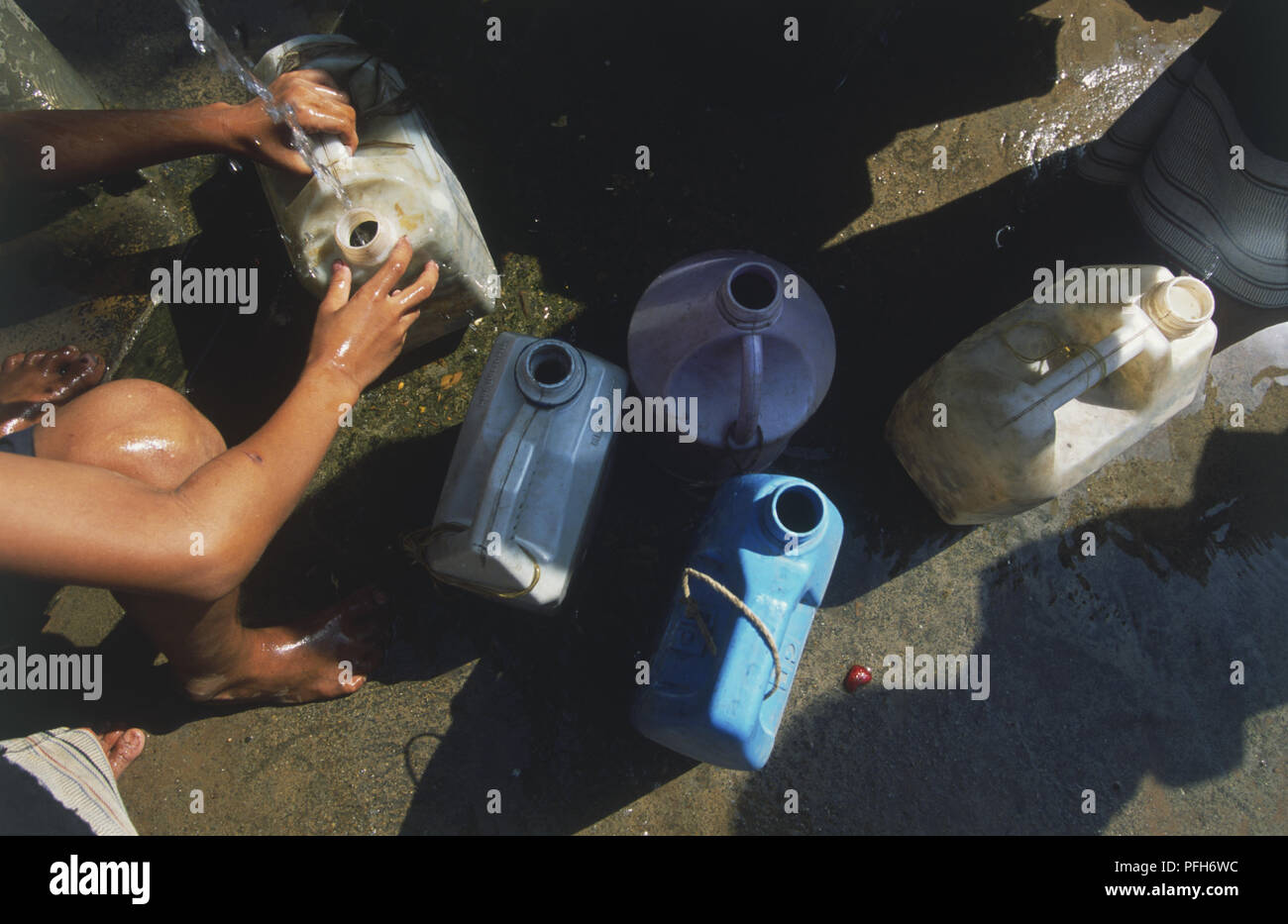 Pouring water from tap into one of four plastic containers, view from ...