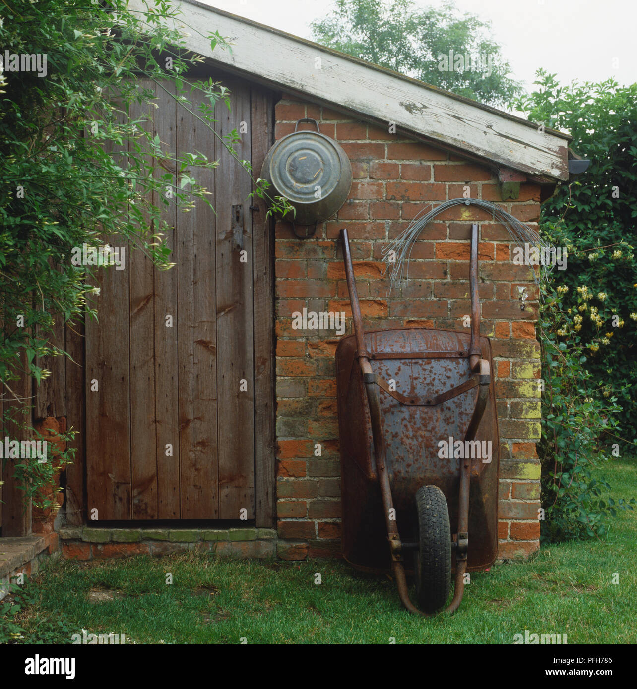 Rusty wheelbarrow leaning against wall of a brick shed Stock Photo - Alamy