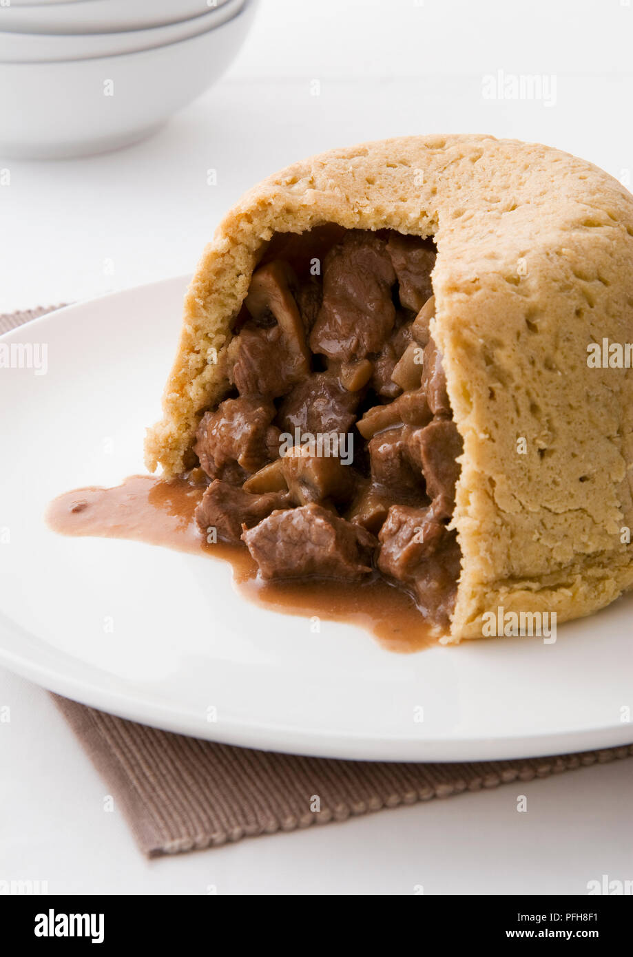 Steak and kidney pudding with stuffing showing, on a plate, close-up ...