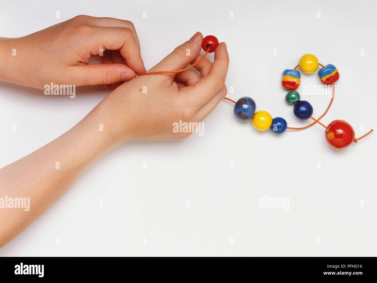 Threading colourful beads onto a piece of string Stock Photo - Alamy