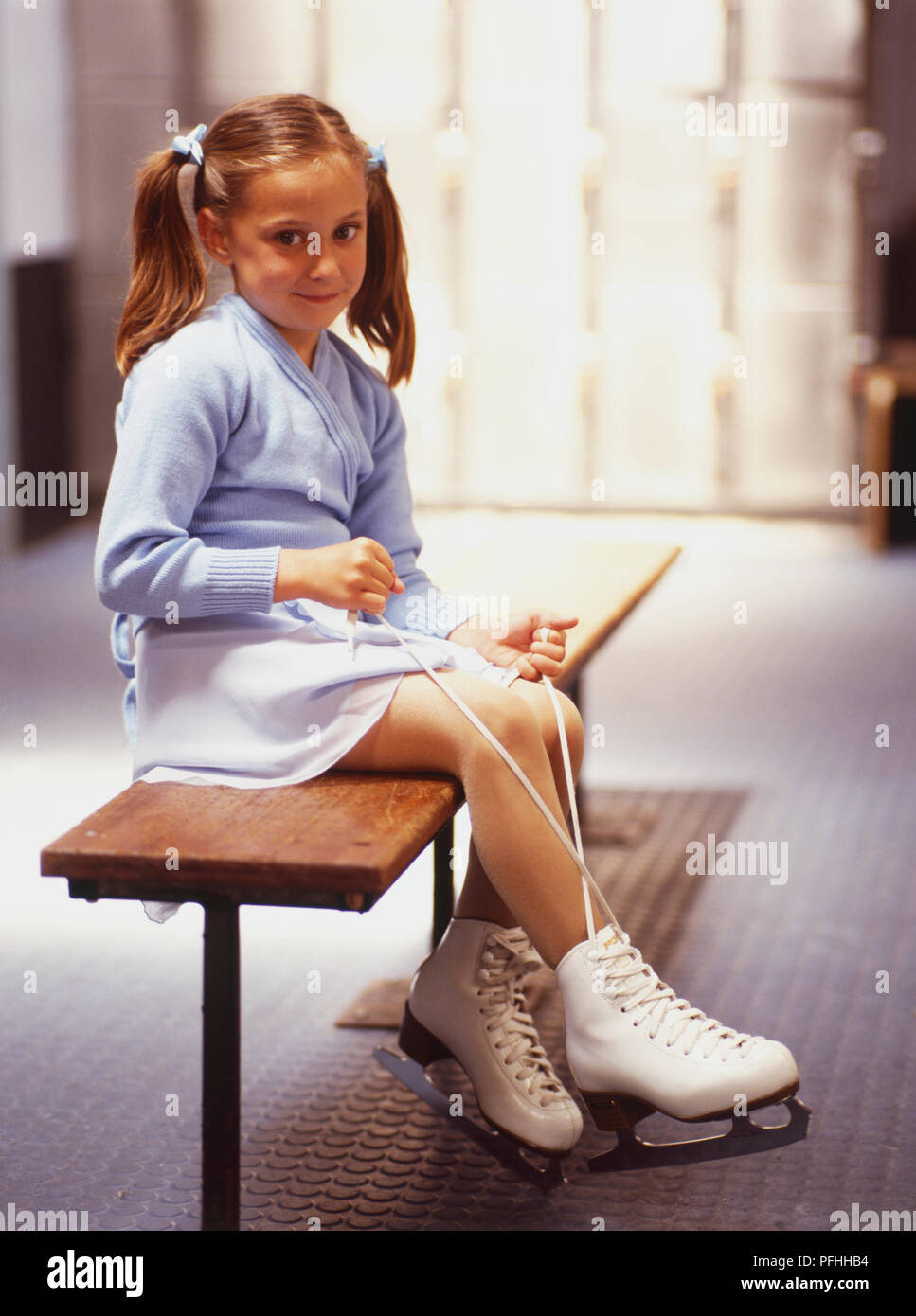 Young ice skater sitting on bench in changing room lacing her white ...