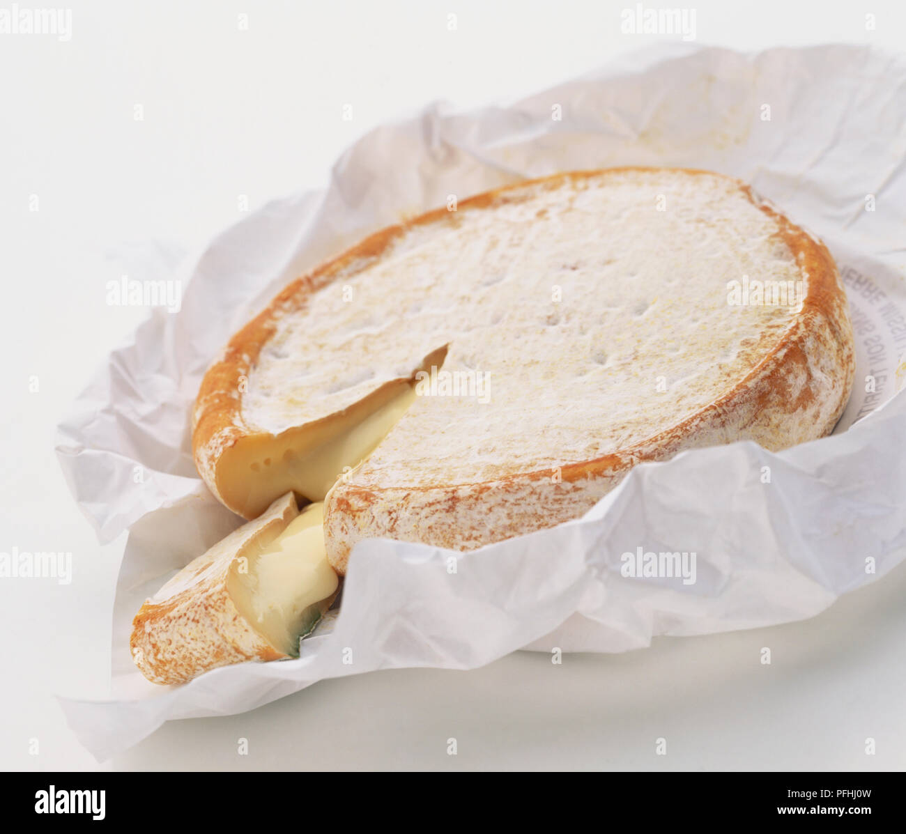 Circular block of cheese with section removed from the centre on paper ...